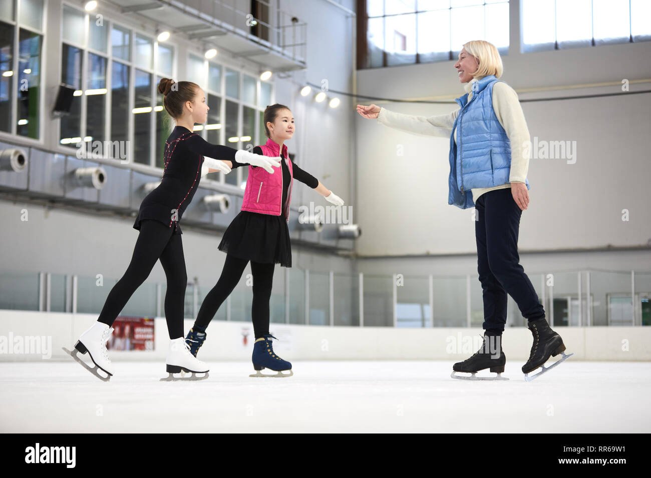 Side view portrait of two girls figure skating on ice rink with female ...