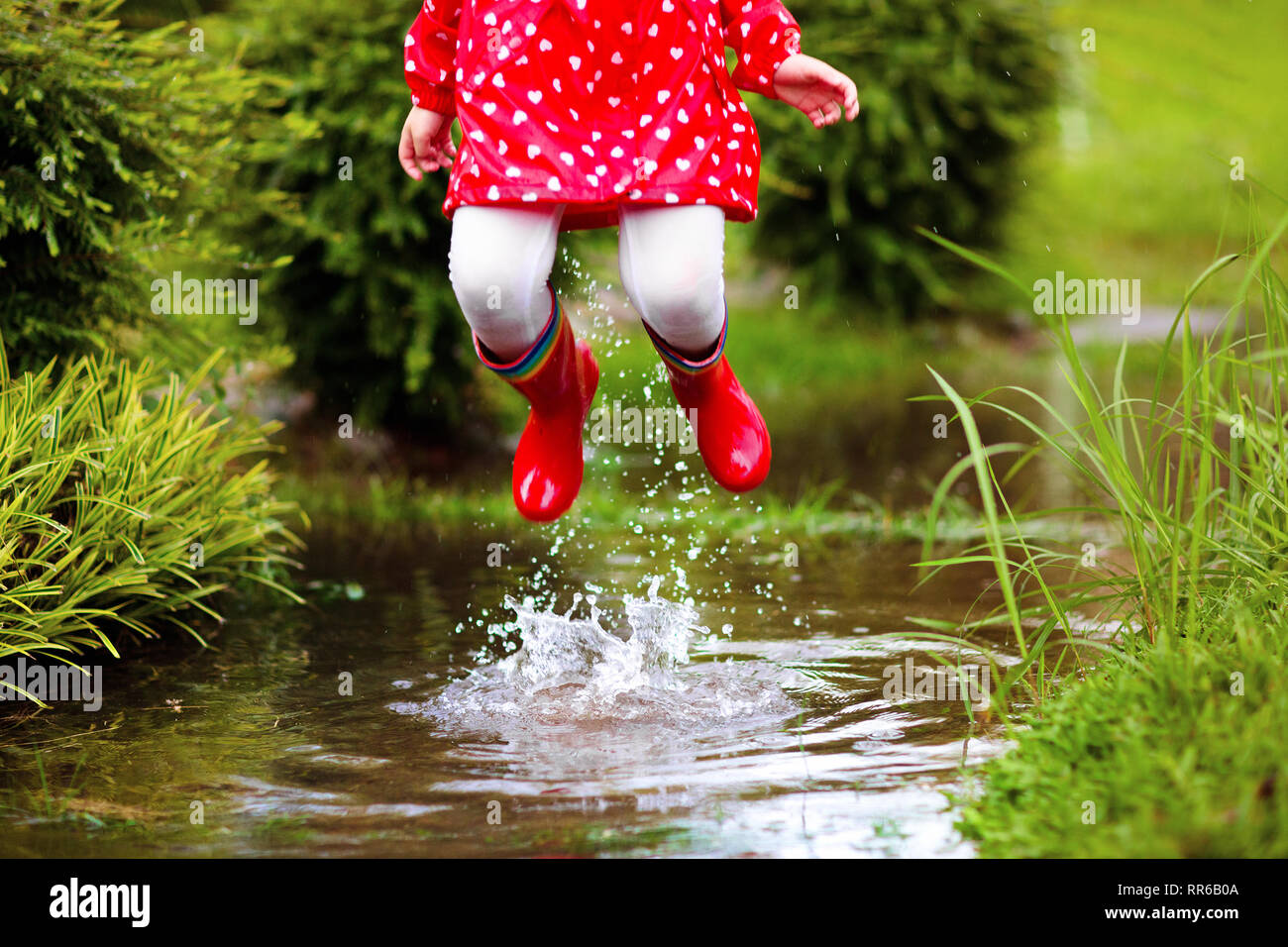 Kid playing in the rain in autumn park. Child jumping in muddy puddle ...