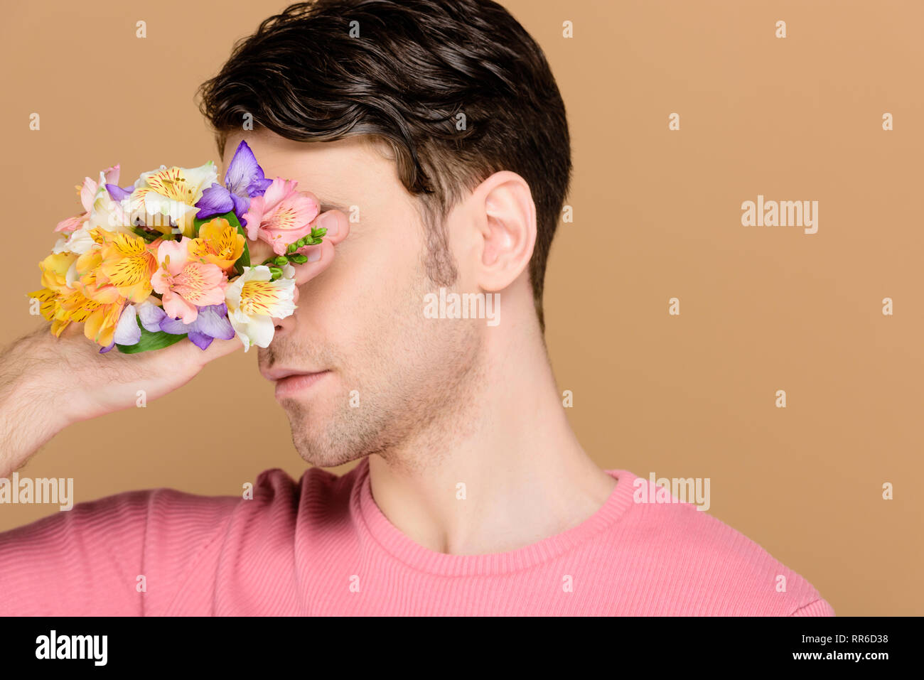 man covering face with alstroemeria flowers on hand isolated on beige ...