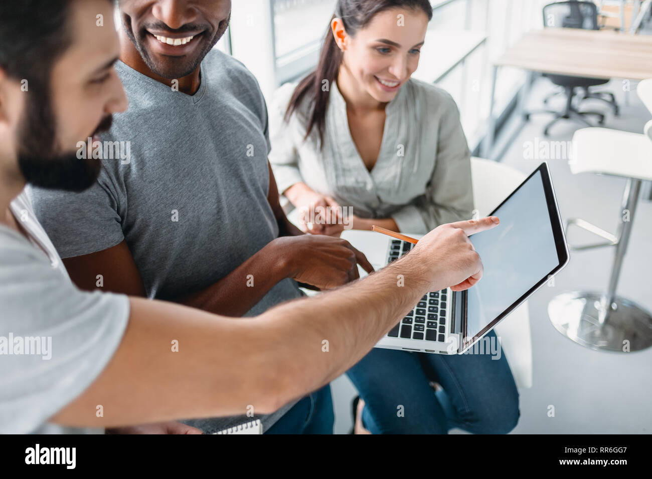 Three young co-workers using laptop and discussing new project at ...