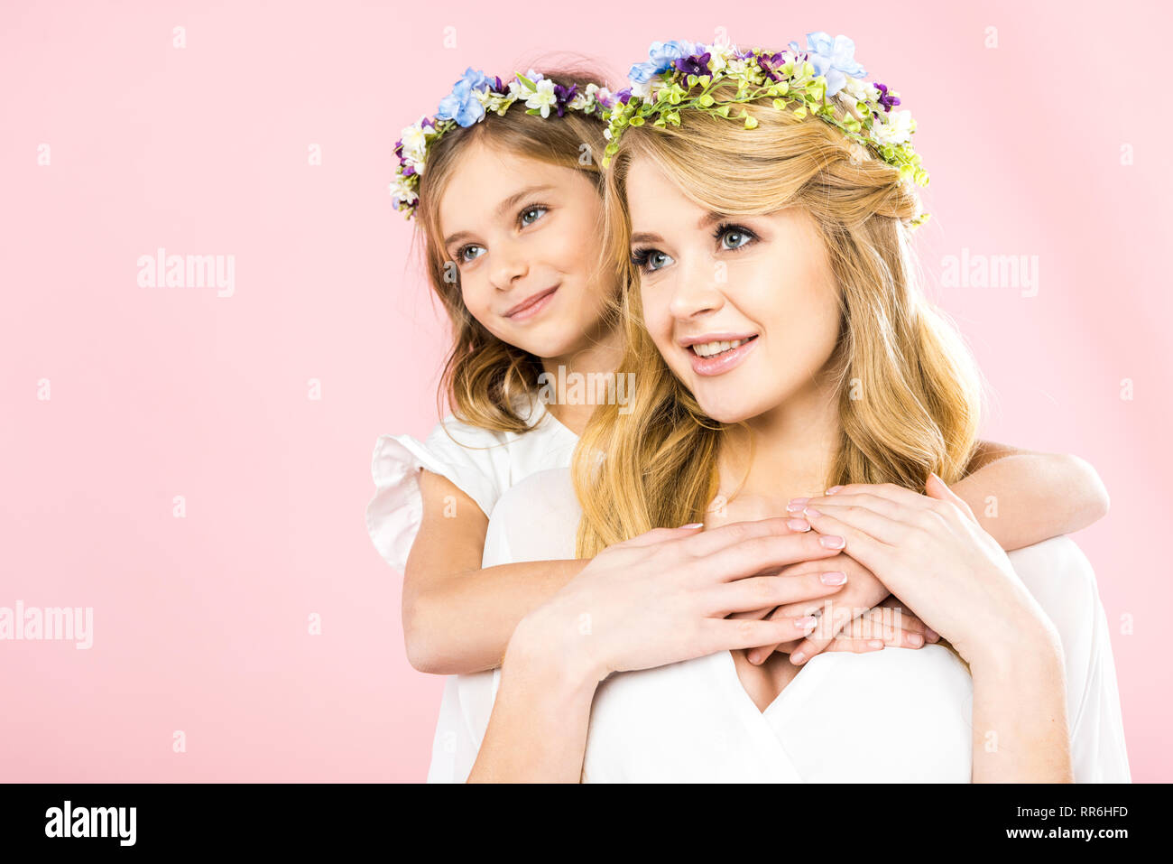 smiling child hugging beautiful mother from back on pink background ...