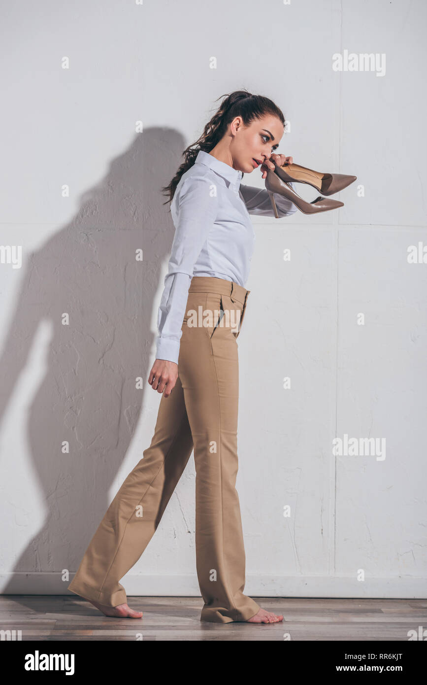 sad woman crying, holding shoes and standing on brown floor near white ...