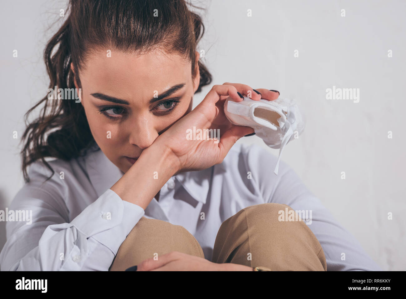sad woman crying and holding baby shoe on white background, grieving ...