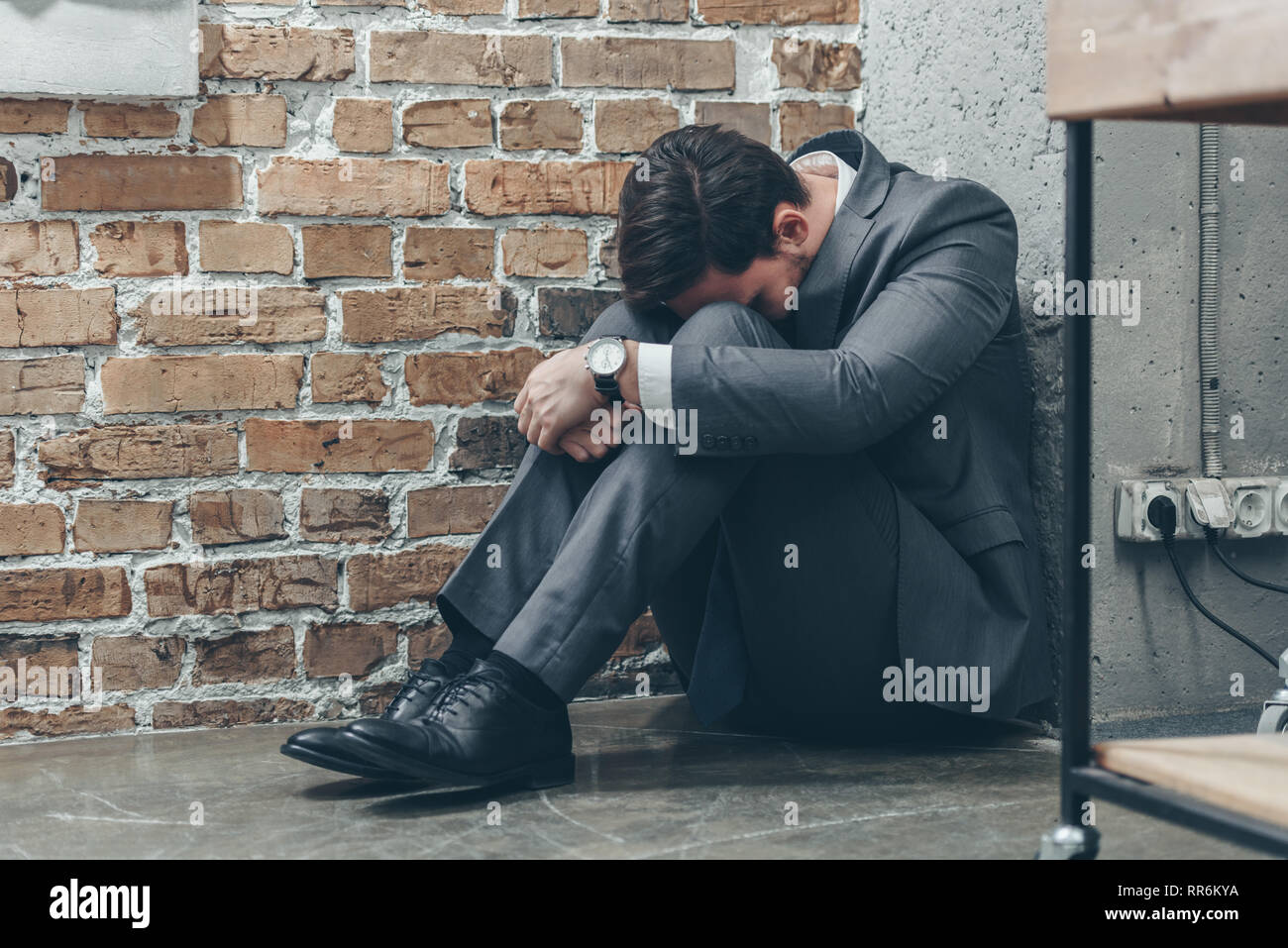 sad man in gray suit sitting on floor and hugging knees on brown ...