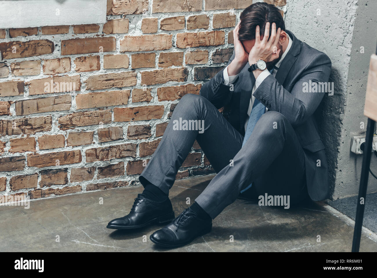 sad man in grey suit sitting in corner on floor and crying on textured ...