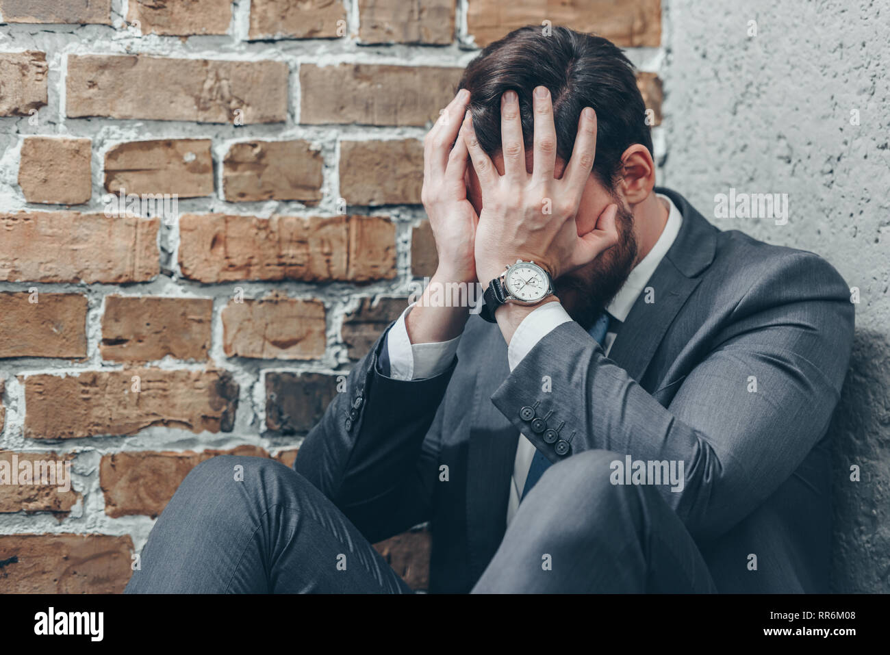 sad man in gray suit sitting and covering face with hands on brown ...