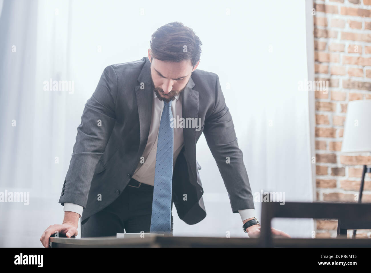sad man in gray suit standing near table and looking at photo in frame ...