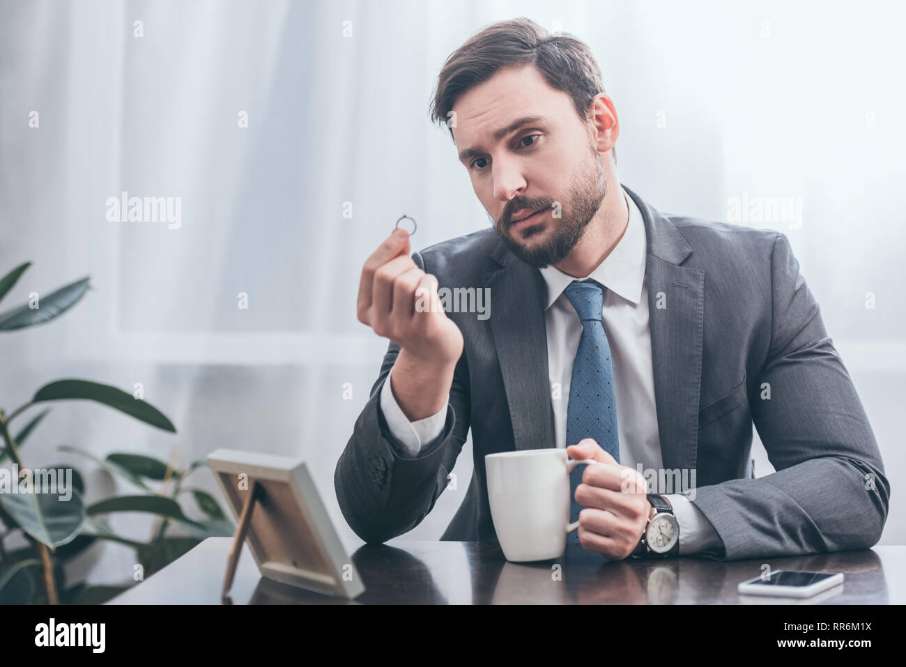 sad man in gray suit sitting at wooden table with smartphone, photo in ...
