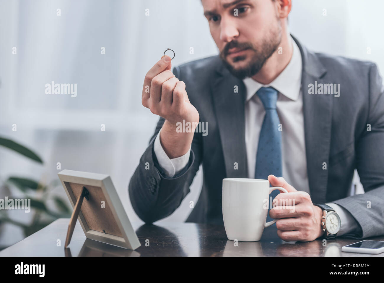 selective focus of sad man in gray suit sitting at wooden table and ...