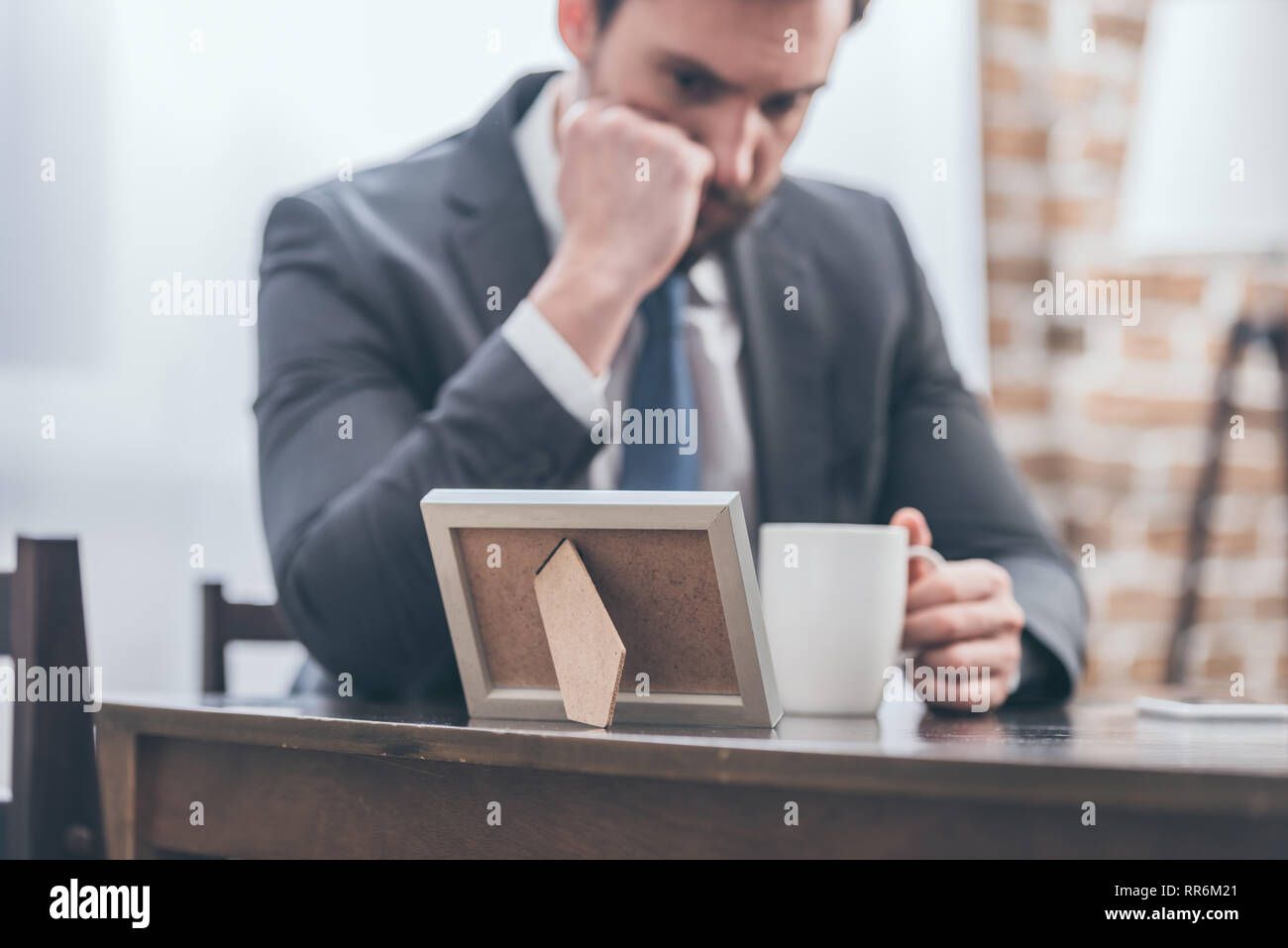 selective focus of upset man in gray suit sitting at wooden table ...
