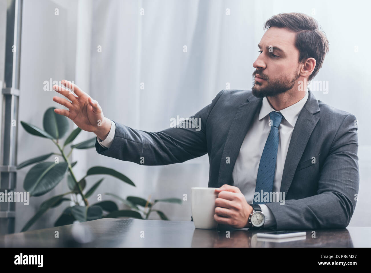 sad man in gray suit sitting at wooden table with smartphone holding ...