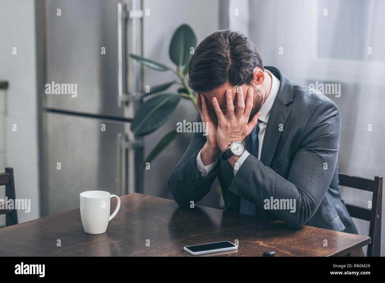 sad man in gray suit sitting at table with smartphone, white cap and ...