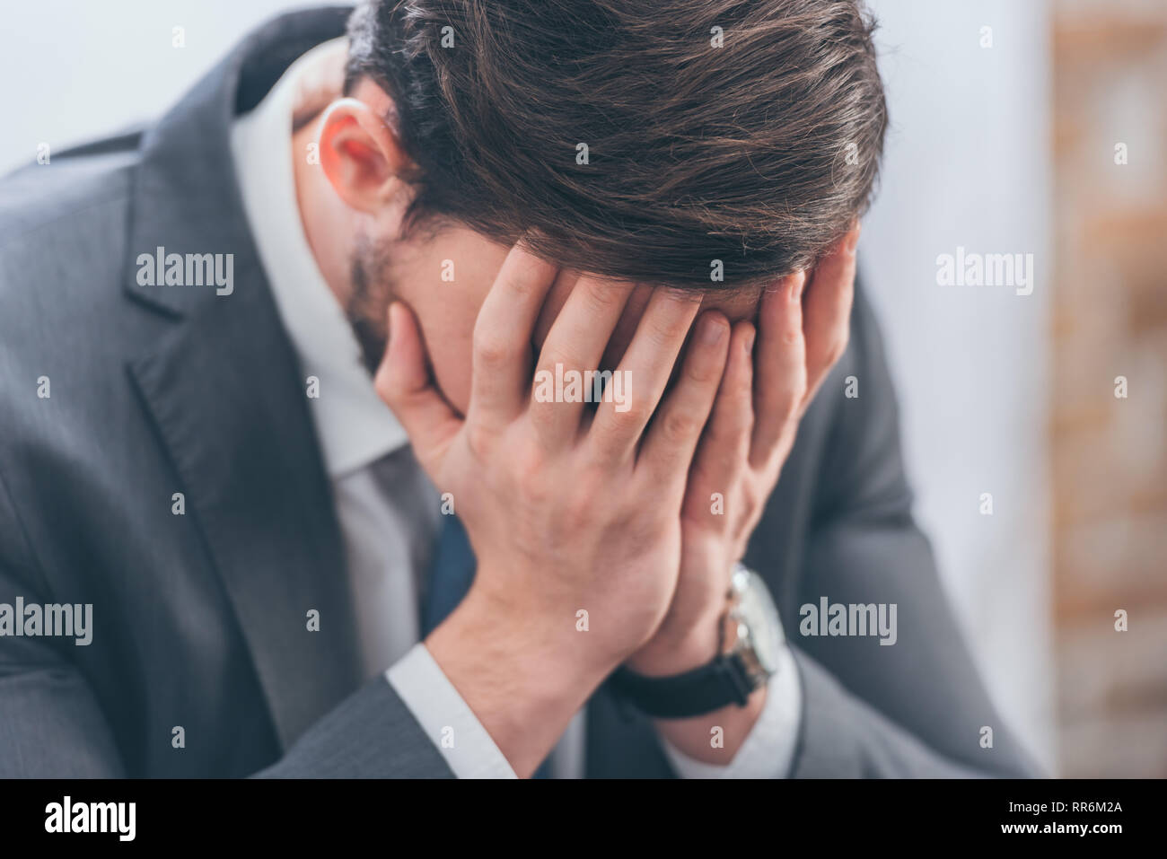 upset man in gray suit covering face with hands in room, grieving ...