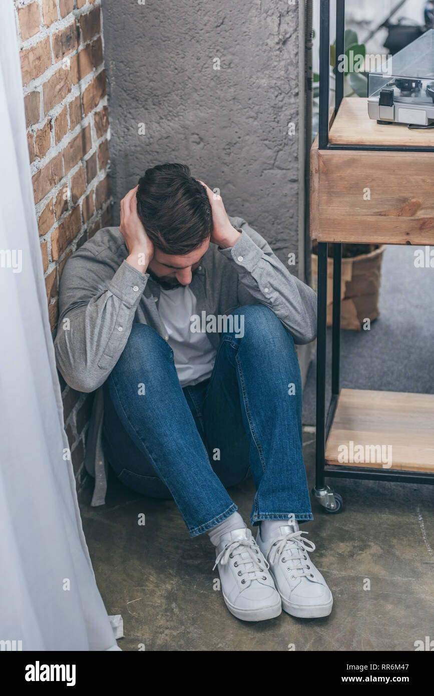 upset man sitting on floor in corner and hugging head on brown textured ...