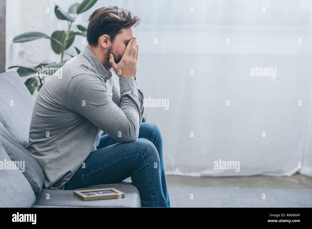 man sitting on grey couch with photo in frame and crying at home ...