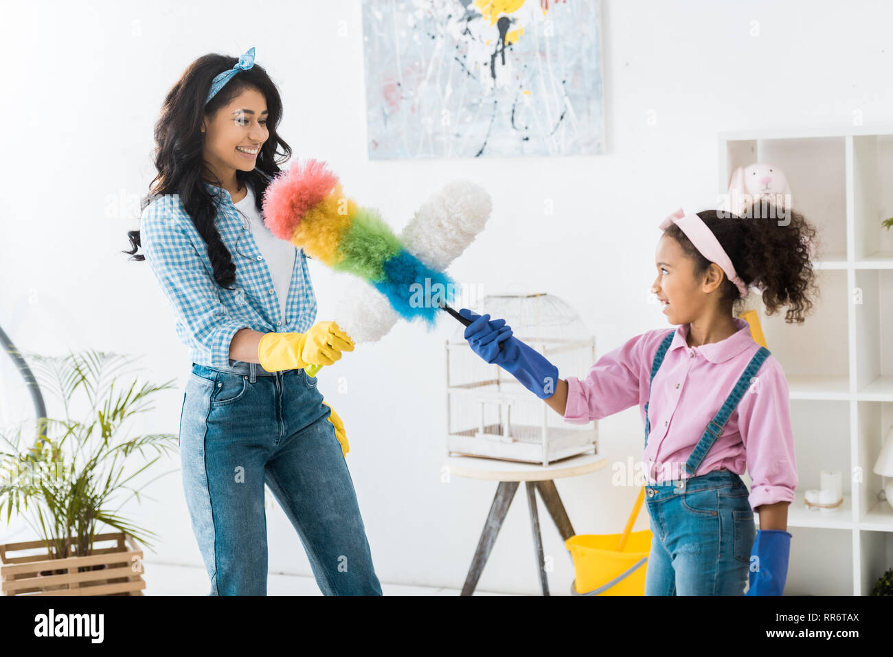 cheerful african american mother and daughter fighting with dusters ...