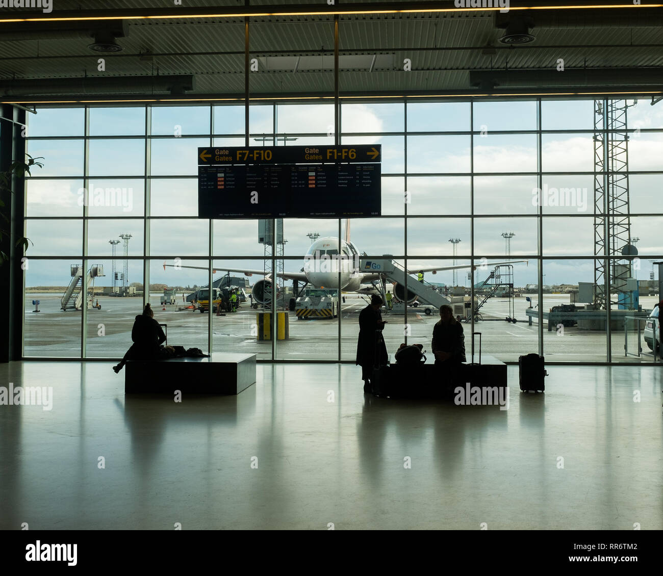 Passengers waiting inside terminal building looking out at parked plane ...