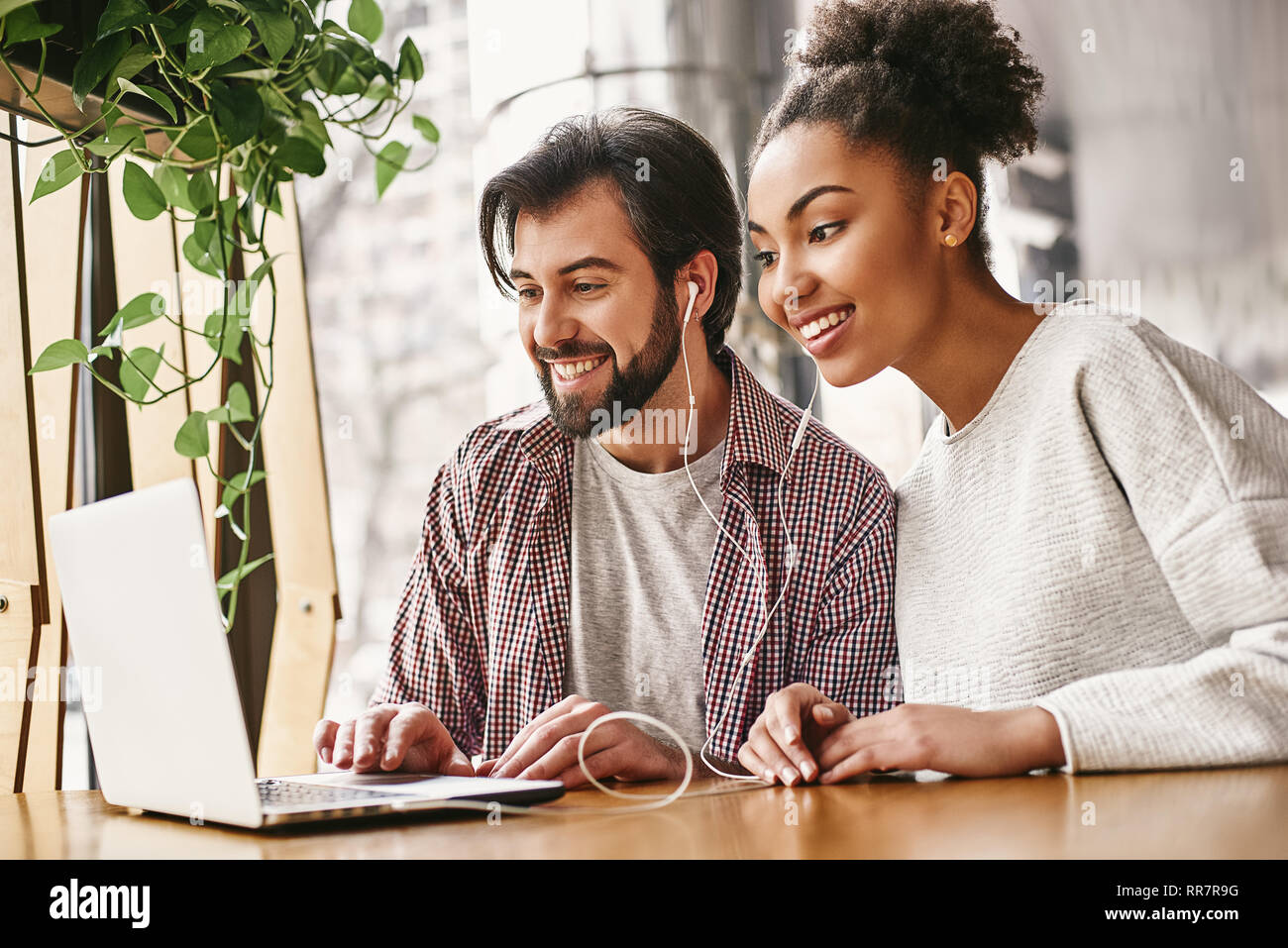 Two cheerful colleagues in office wearing earphones co-working while ...