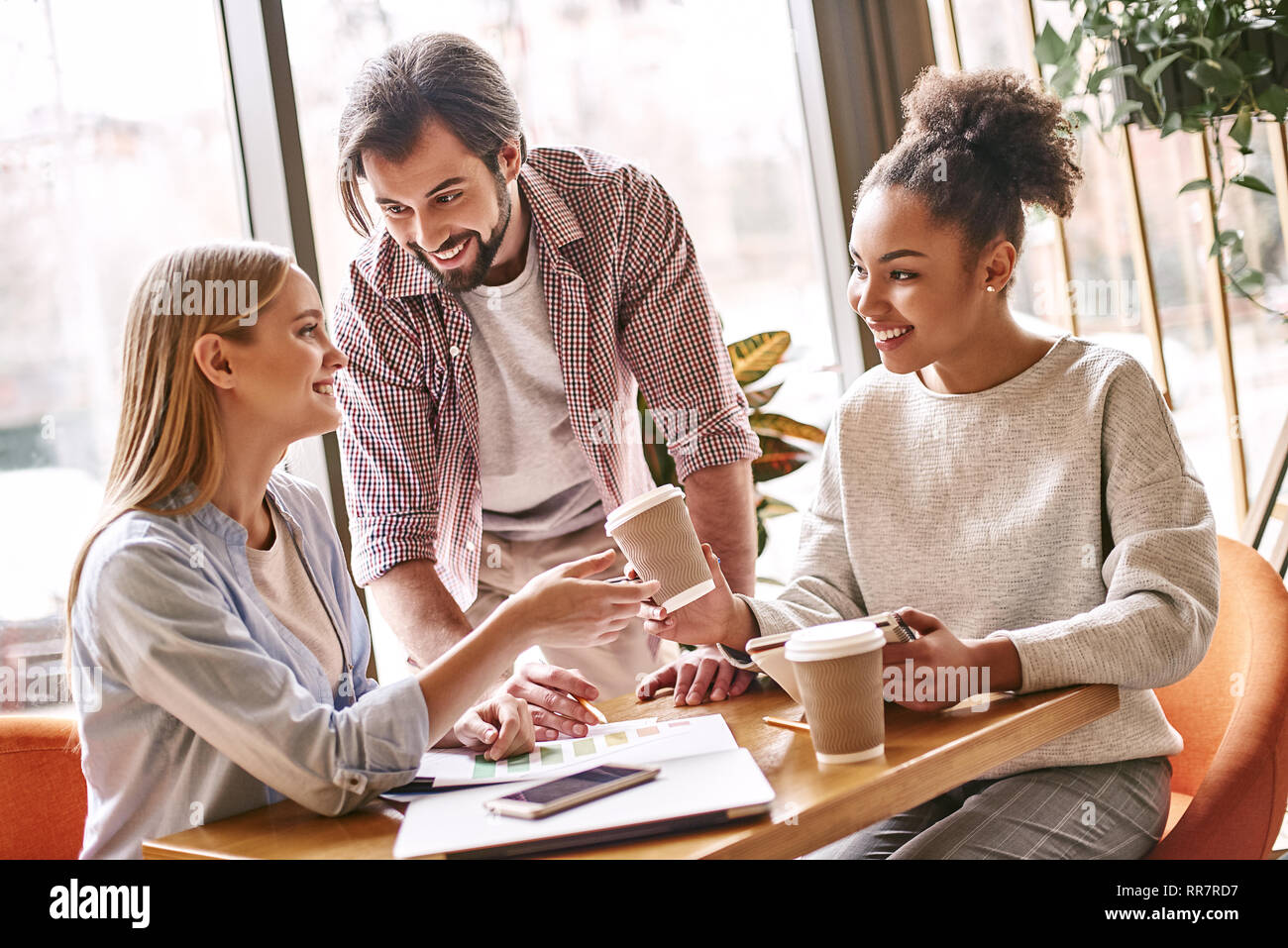 Three young successful business people in casual clothes drink coffee ...
