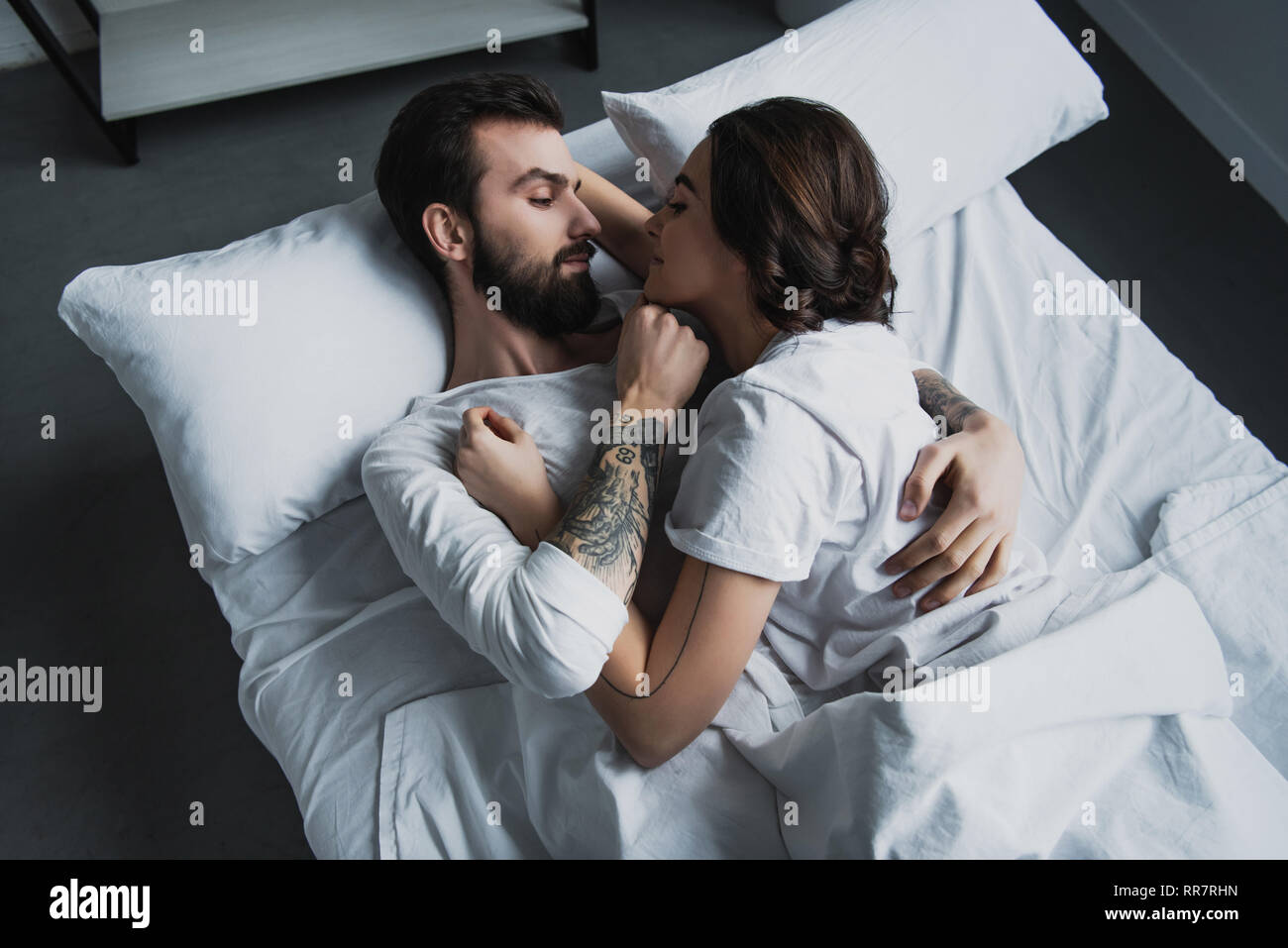 attractive young couple in pajamas embracing while lying in bed at home ...