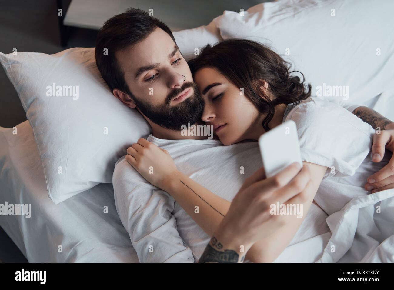 handsome man using smartphone while woman sleeping in bed Stock Photo ...