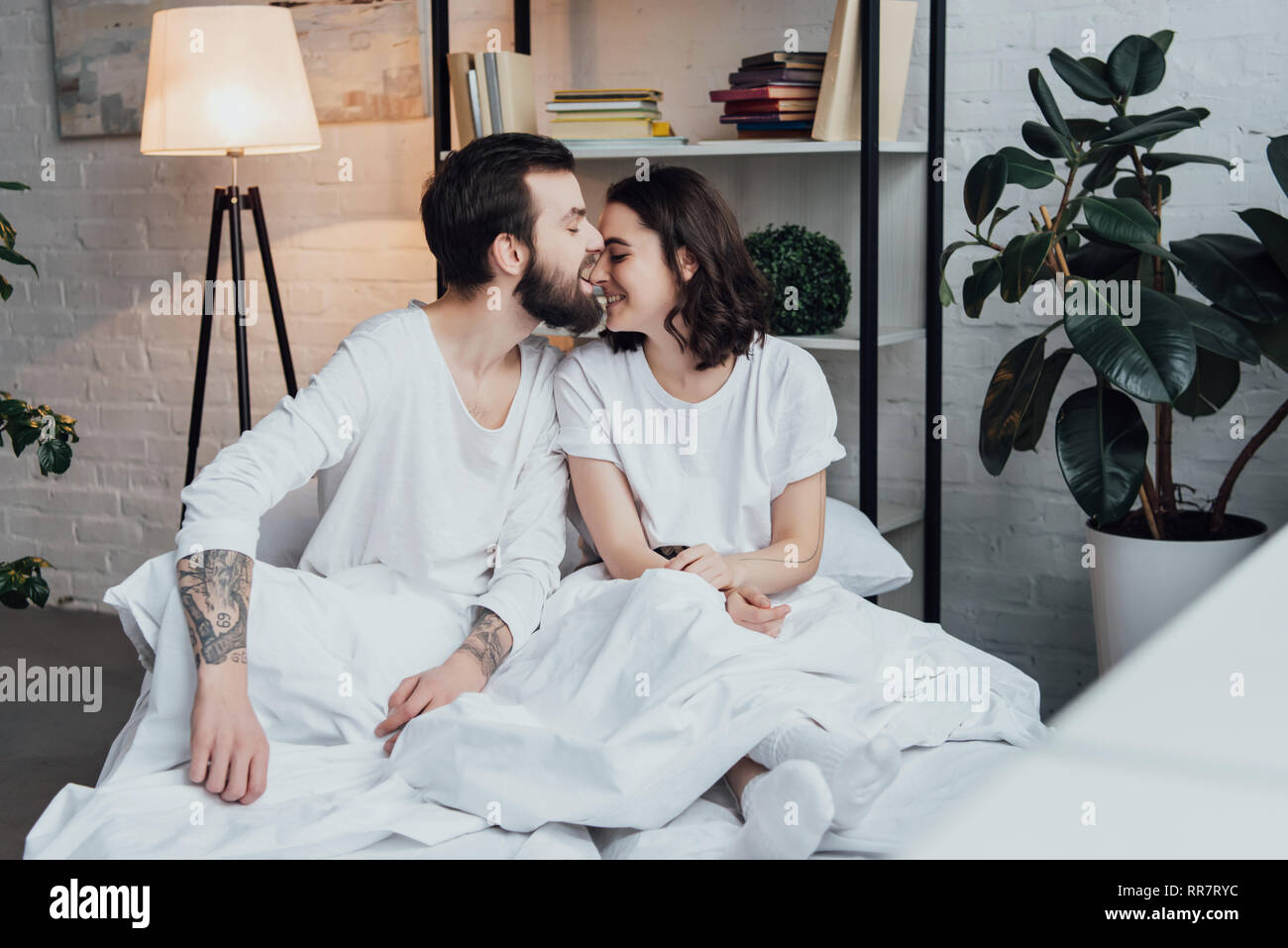 handsome bearded man biting nose of smiling woman at home in bed Stock ...