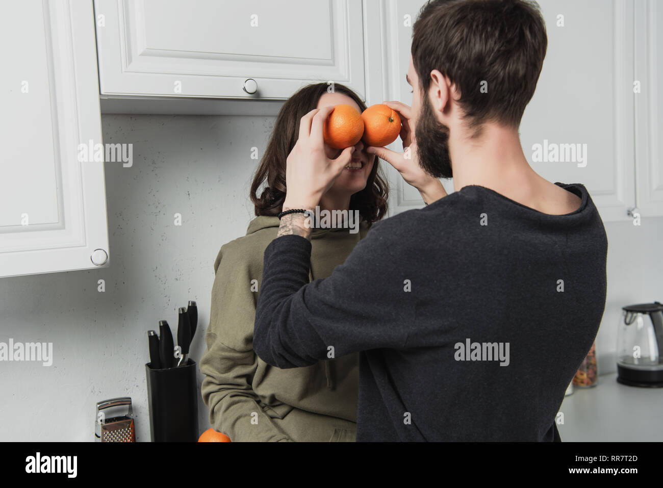 back view of man holding oranges in front of face of woman in kitchen ...