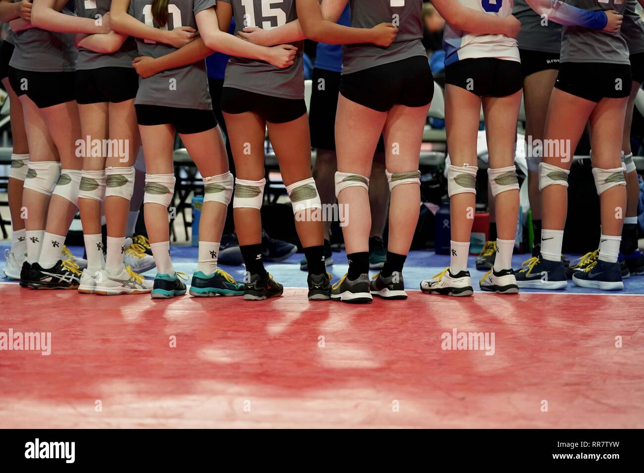 A group of female volleyball lock arms in unity as they form a huddle ...