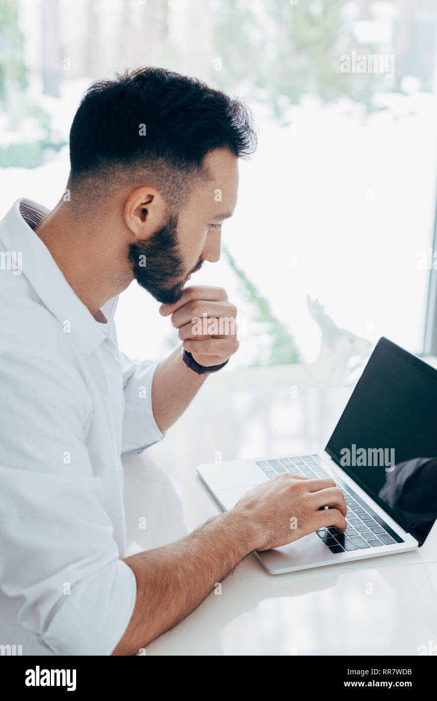 Young man touching beard while typing on laptop keyboard Stock Photo ...