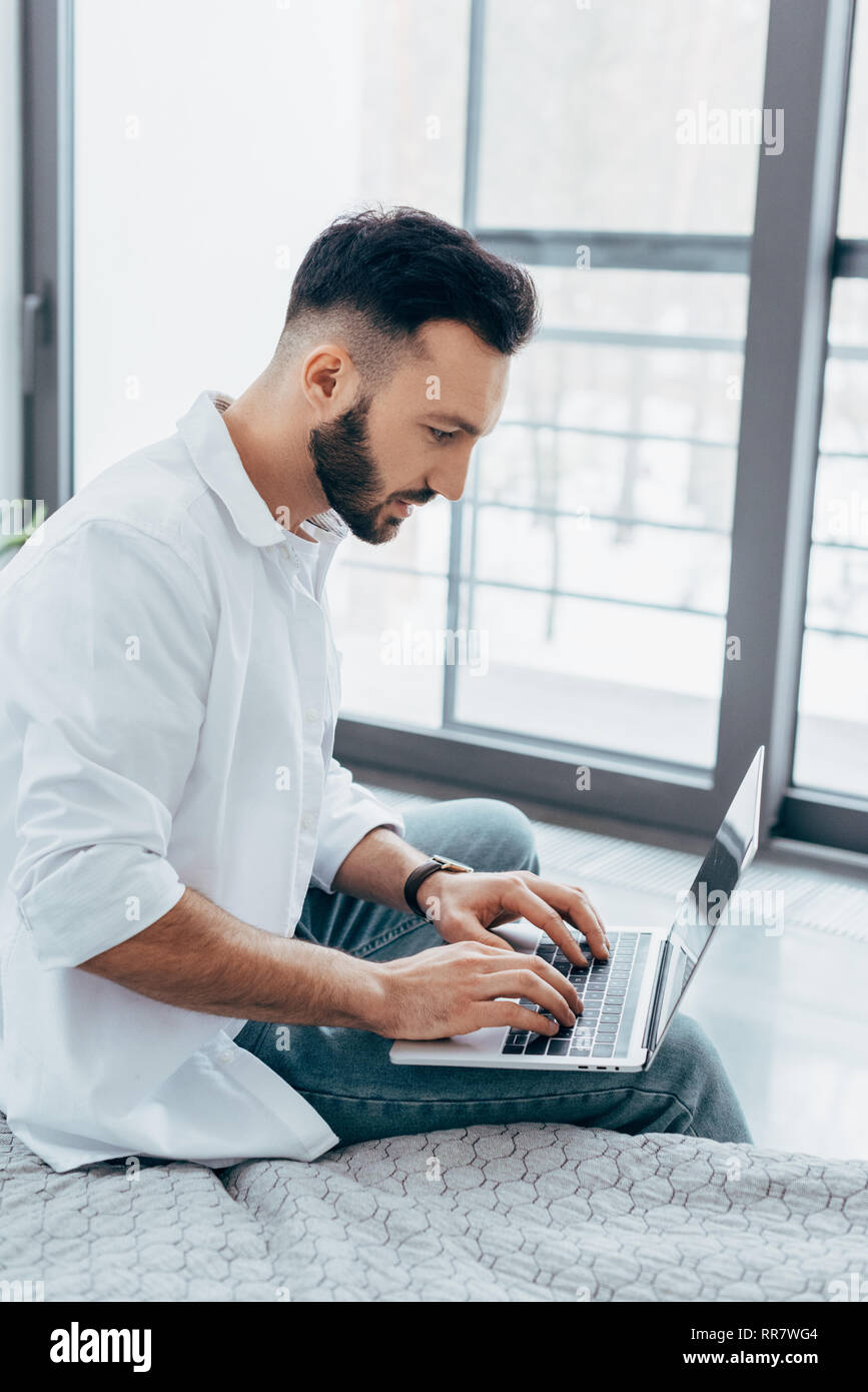 Concentrated handsome man typing on laptop keyboard in bedroom Stock ...