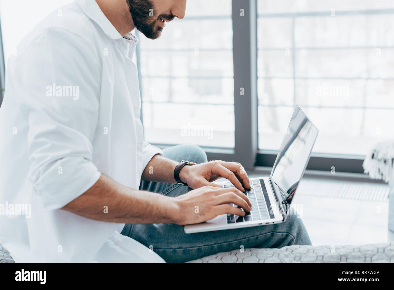 Partial view of man in white shirt and jeans typing on laptop keyboard Stock Photo - Alamy