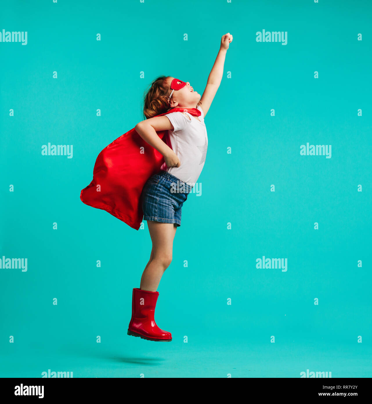 Adorable girl in red superhero costume and mask jumping with a arm ...