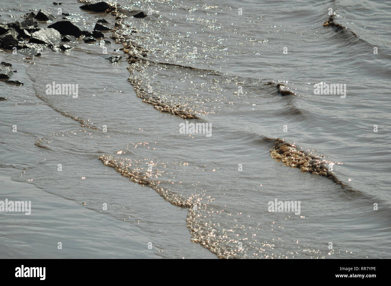 slow waves at a sandy and rocky beach with sunlight Stock Photo - Alamy