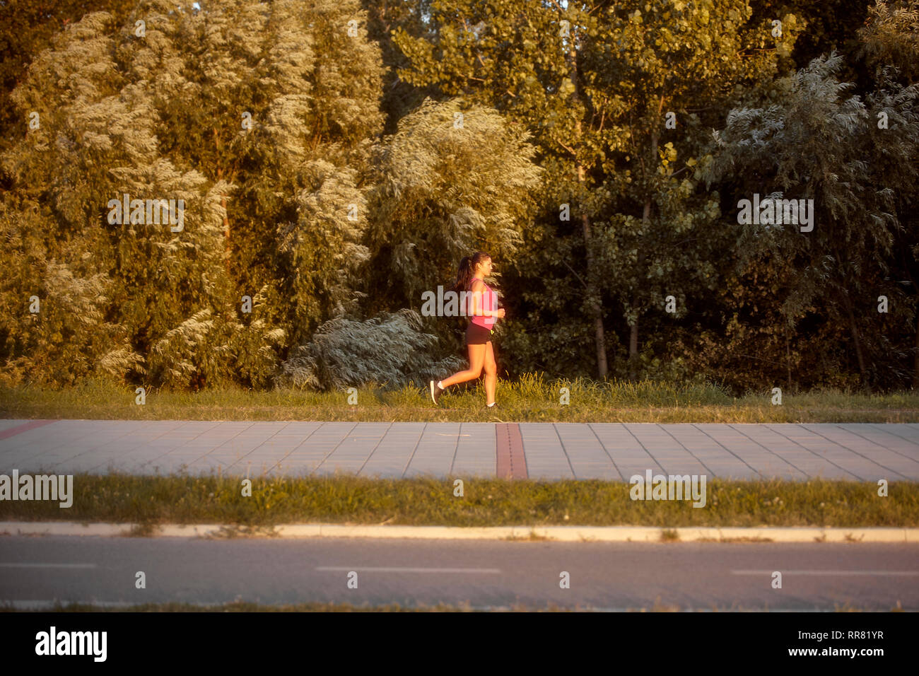 one young woman, running alone outdoors on a asphalt track. Surrounded ...