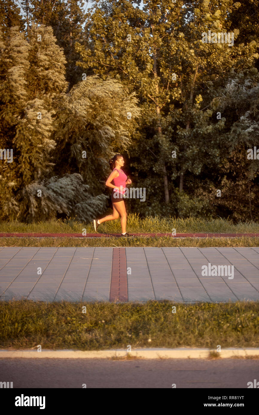 one young woman, running alone outdoors on a asphalt track. Surrounded ...