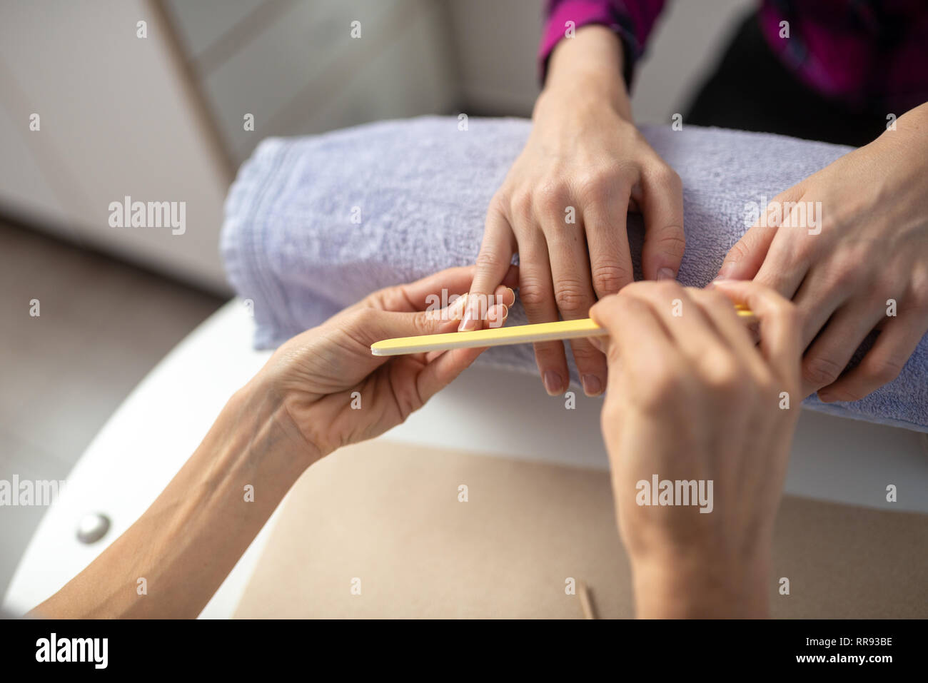 Over the shoulder view of professional manicurist filing nails of a ...