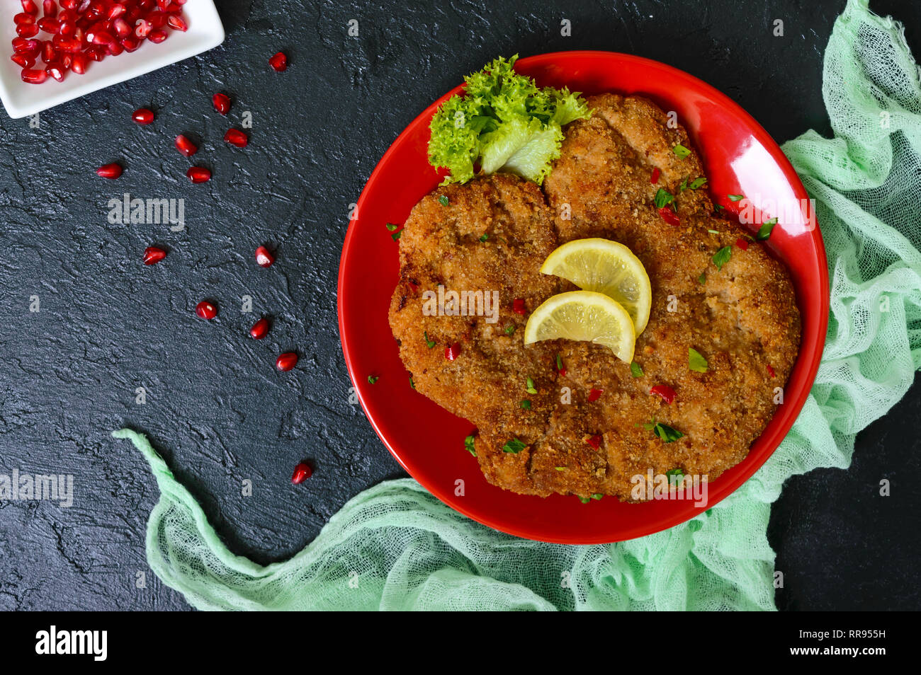 Large Viennese schnitzel on a red plate with lemon on a black ...