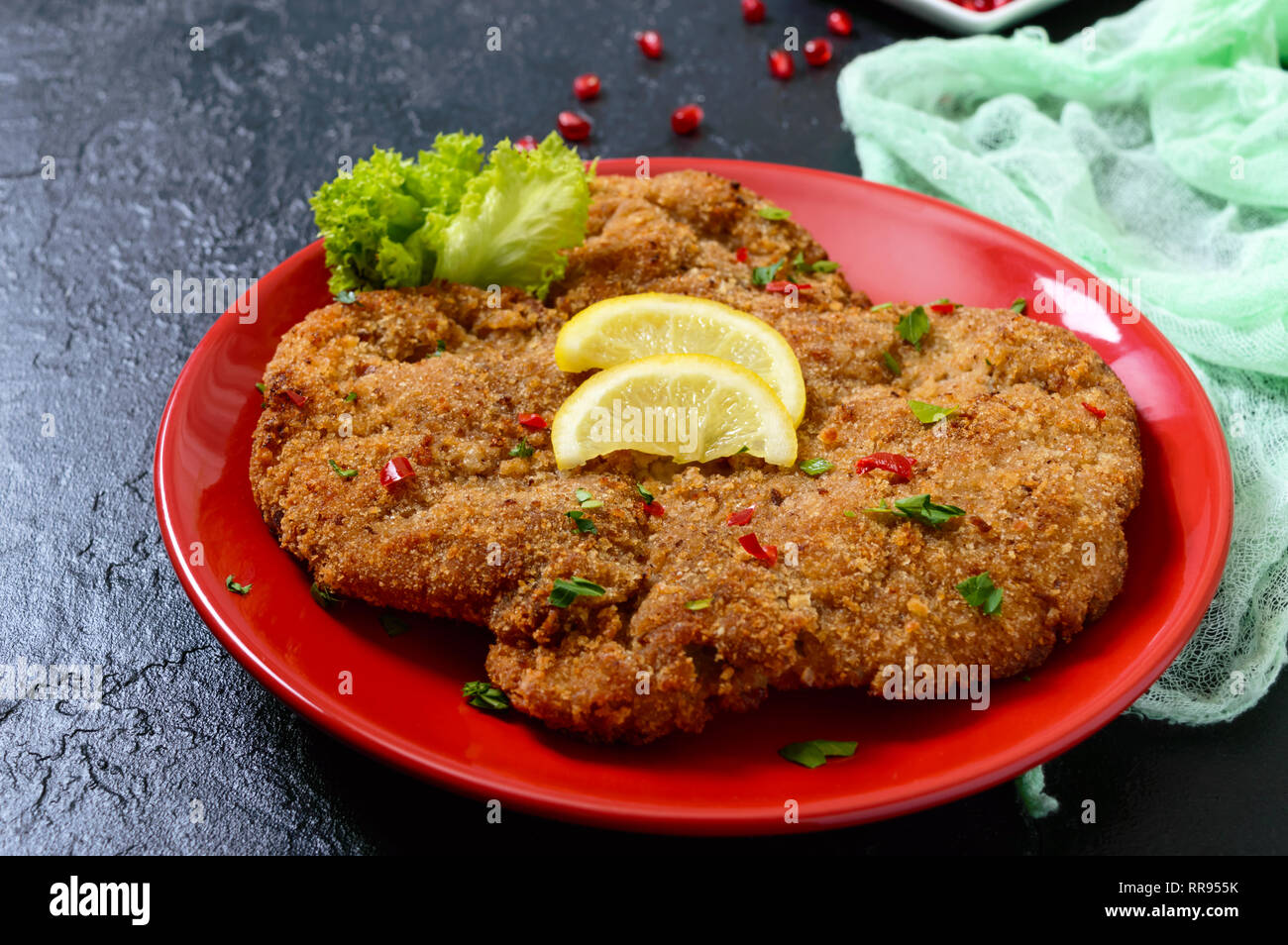 Large Viennese schnitzel on a red plate with lemon on a black ...
