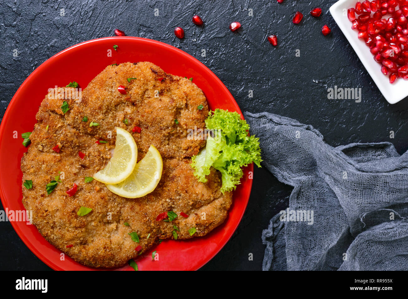 Large Viennese schnitzel on a red plate with lemon on a black ...