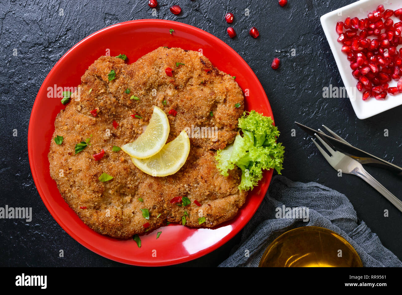 Large Viennese schnitzel on a red plate with lemon on a black ...