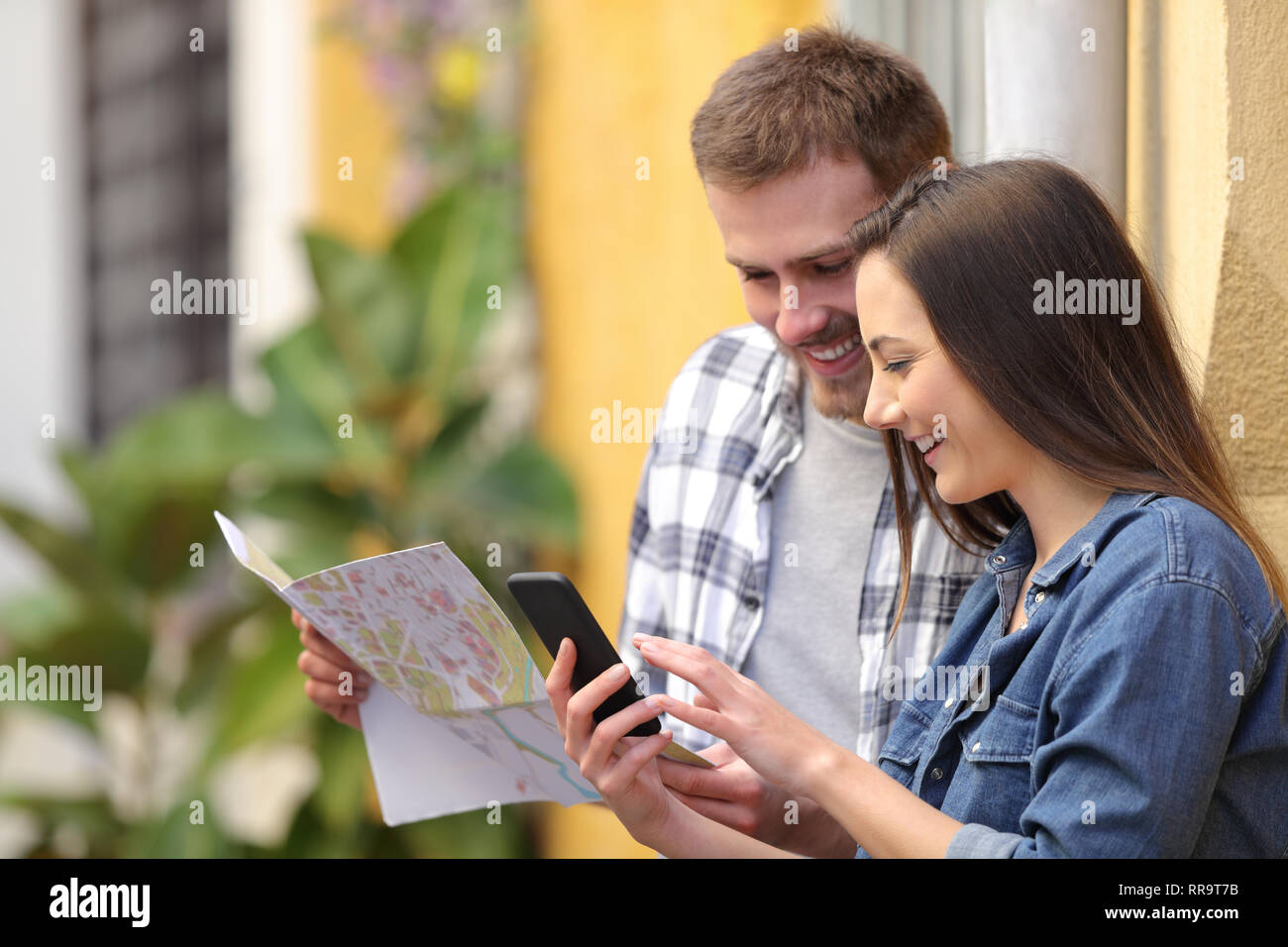 Two happy tourists checking map and smart phone on vacation in the ...