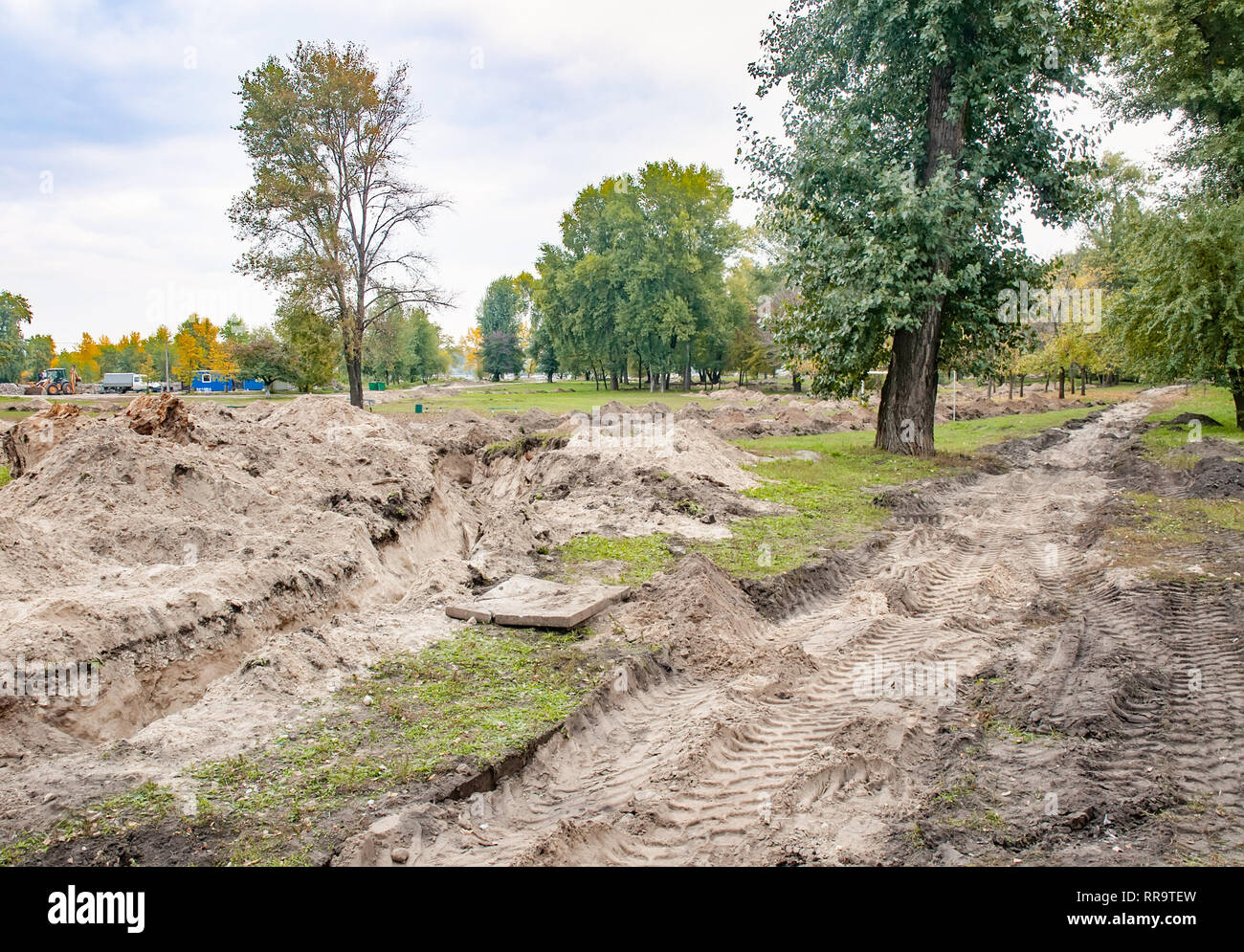 A trench in the sandy ground for laying a pipe in the park, under the ...