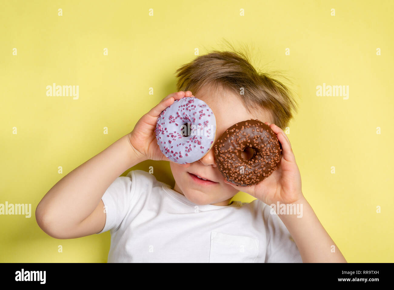 Boy holding donuts by this eyes, bright background Stock Photo - Alamy