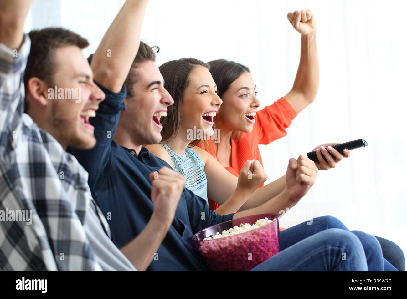 Four excited friends watching tv celebrating success sitting on a coucn ...