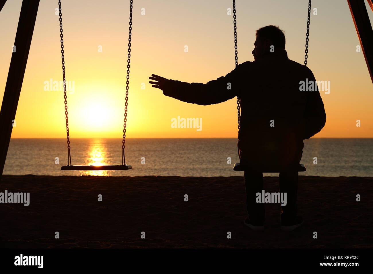 Back view backlighting silhouette of a man sitting on swing alone ...