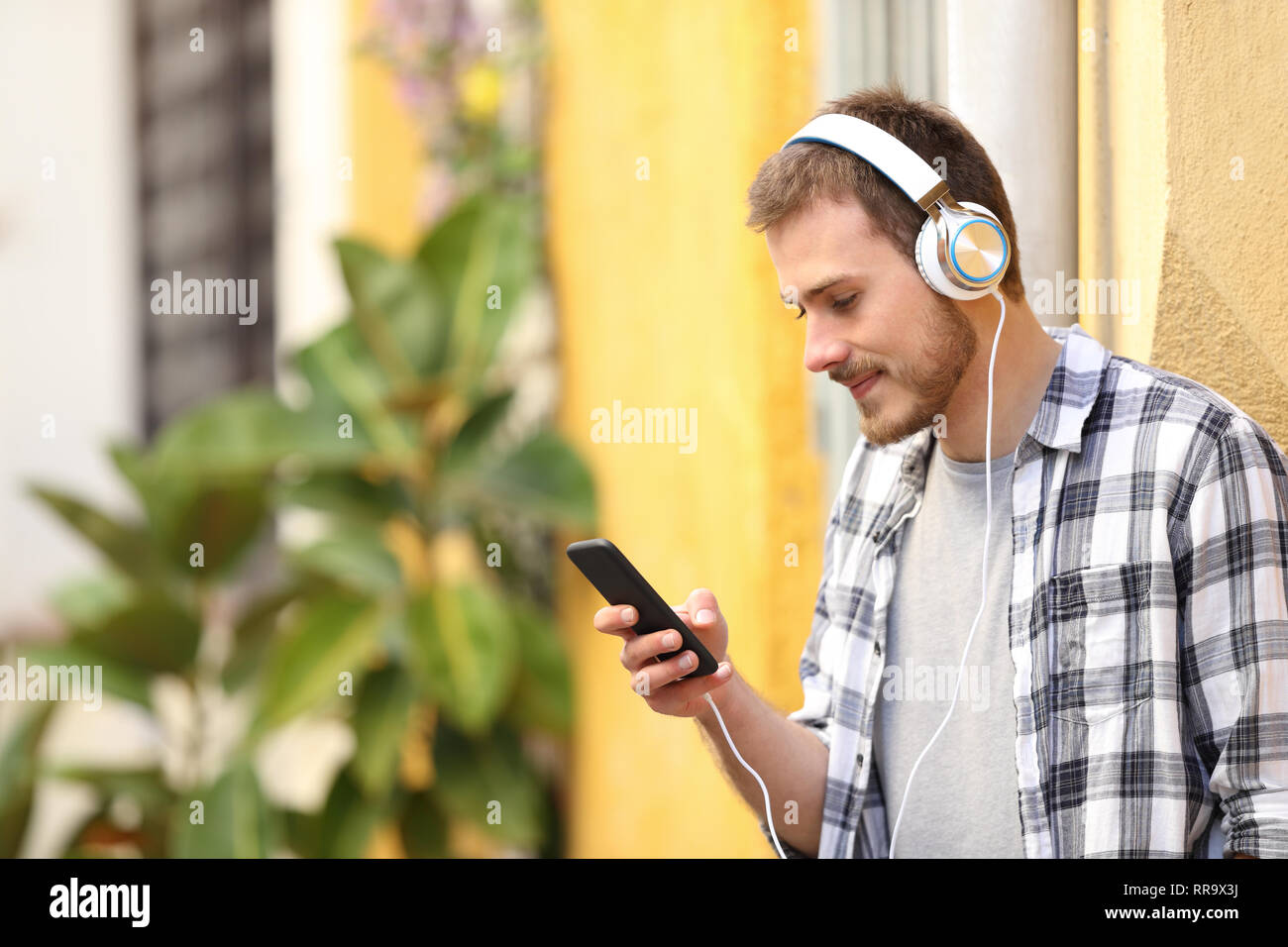 Serious man listening to music from smart phone and headphones standing ...
