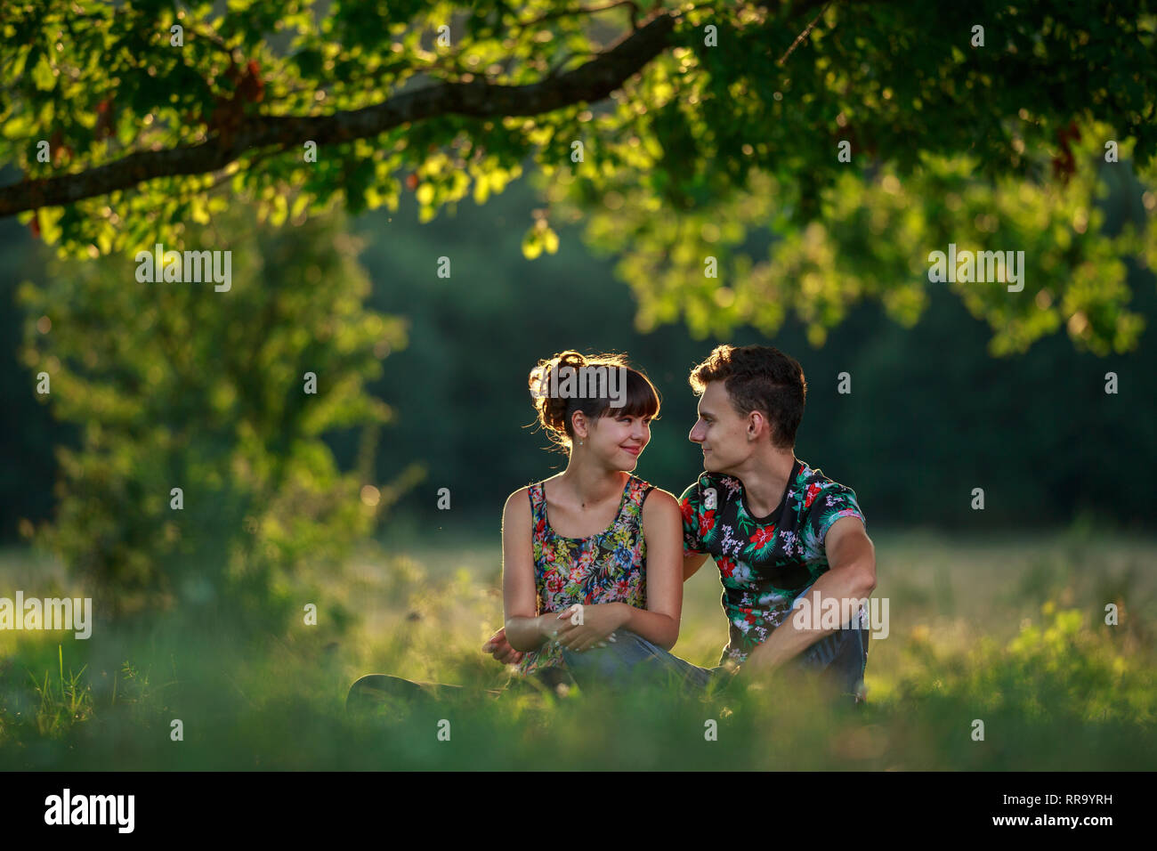 Young couple sitting under a tree Stock Photo - Alamy