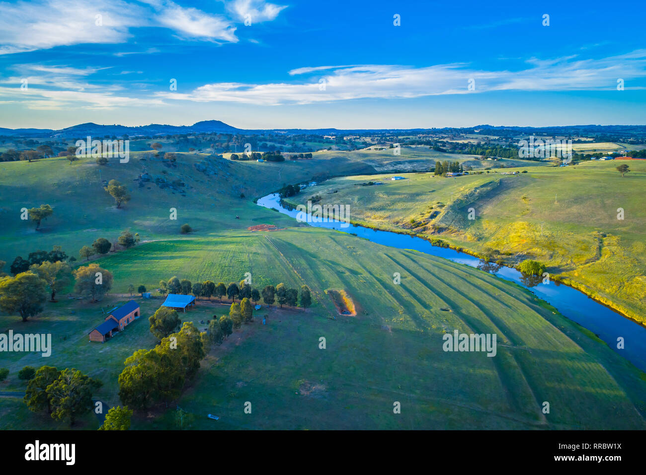 River flowing through countryside grasslands at sunset - aerial view ...
