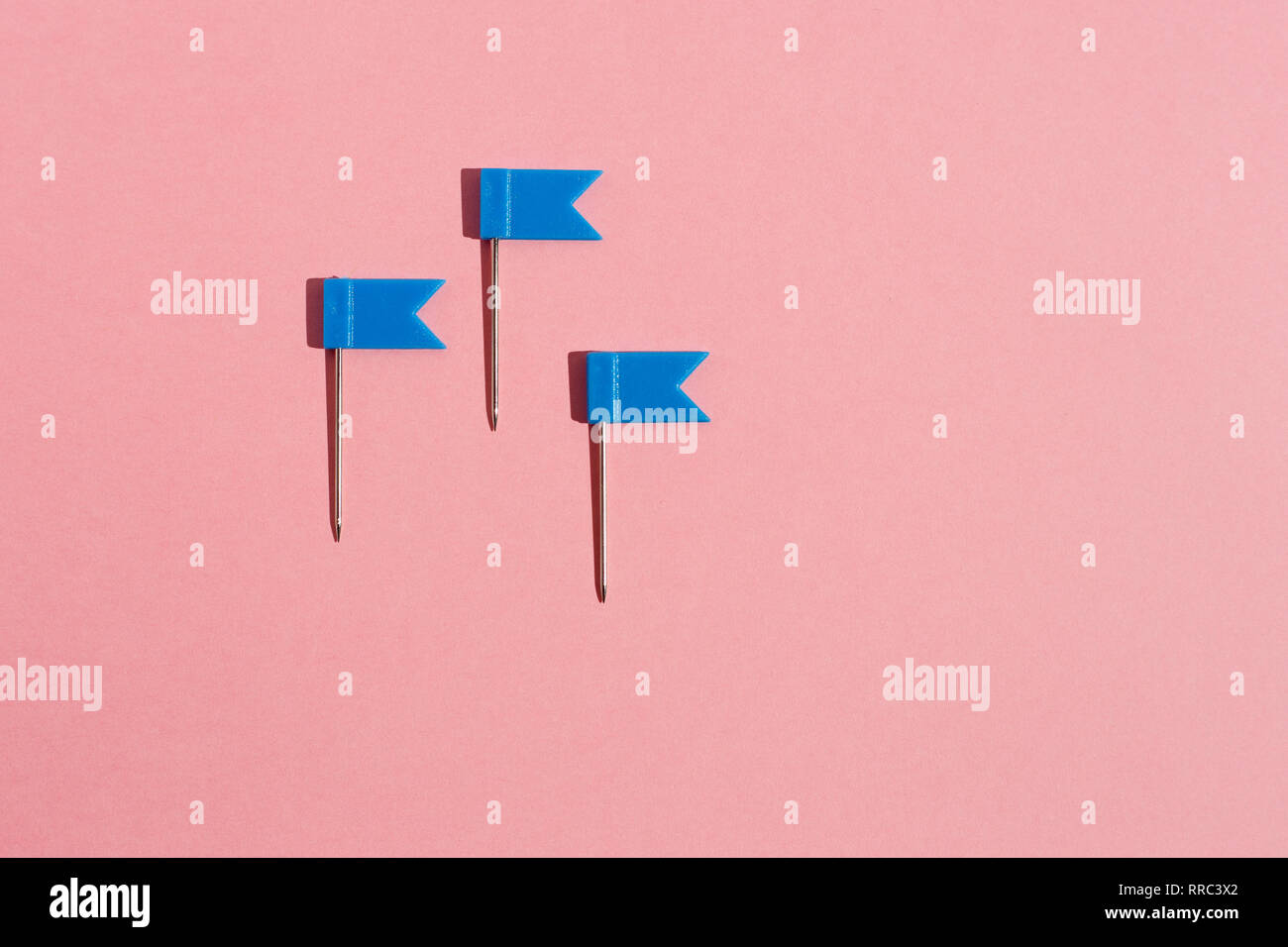 Three blue little flag pins on a pink background. View from above Stock ...