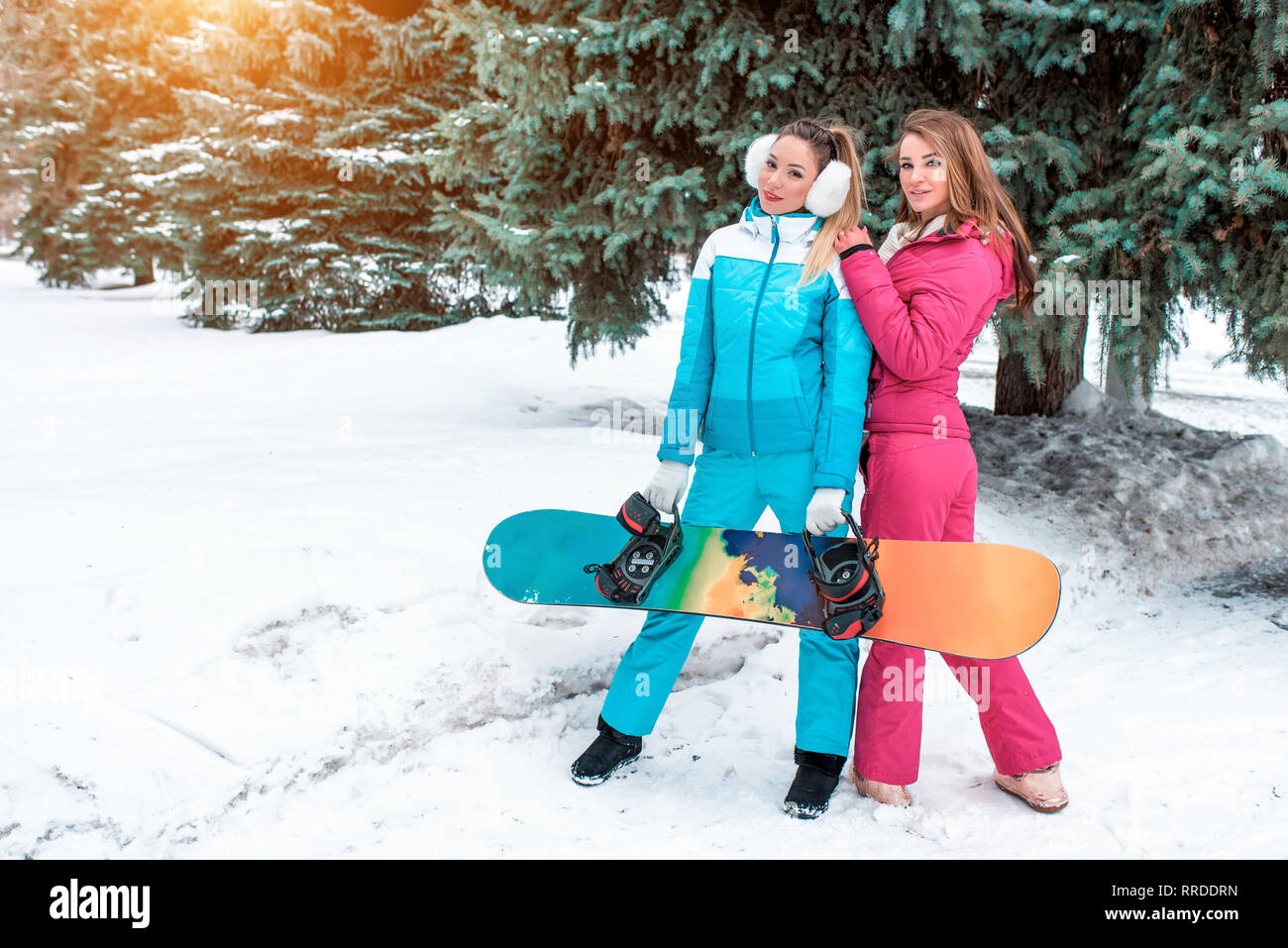 Two girls girlfriends on snowboards, posing on background of green ...